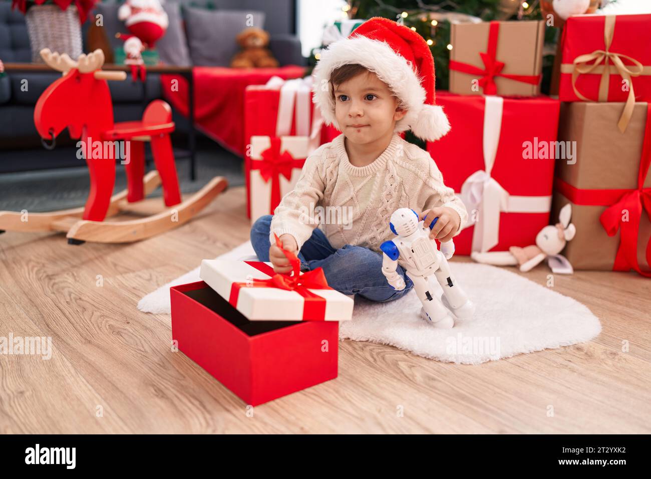 Adorable hispanic boy unpacking robot toy sitting on floor by christmas ...