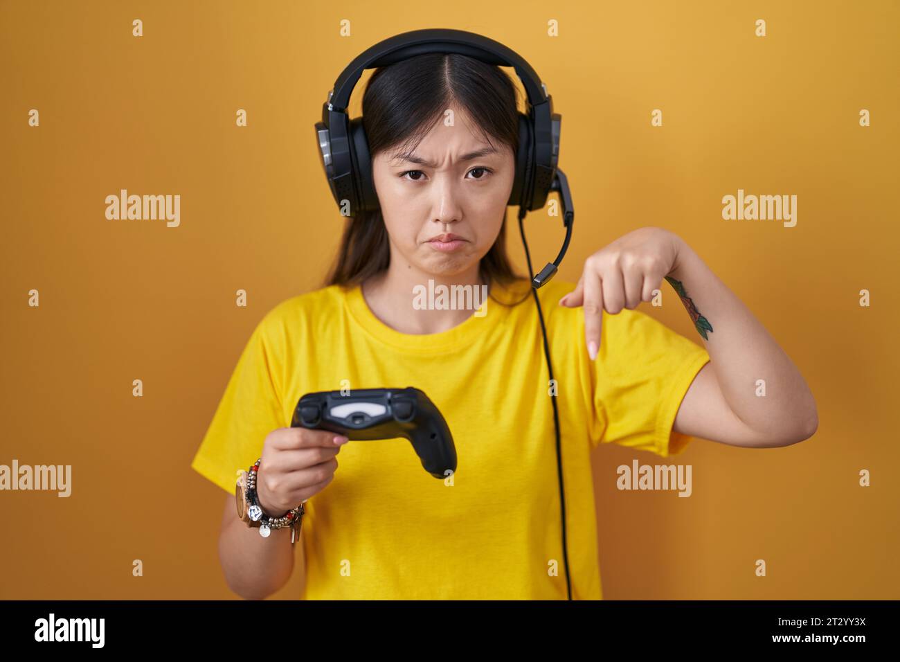 Chinese young woman playing video game holding controller pointing down ...