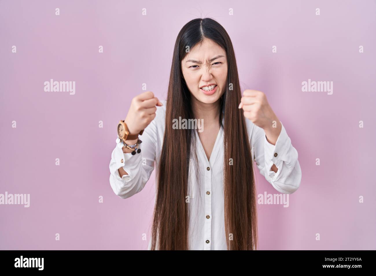 Chinese young woman standing over pink background angry and mad raising ...
