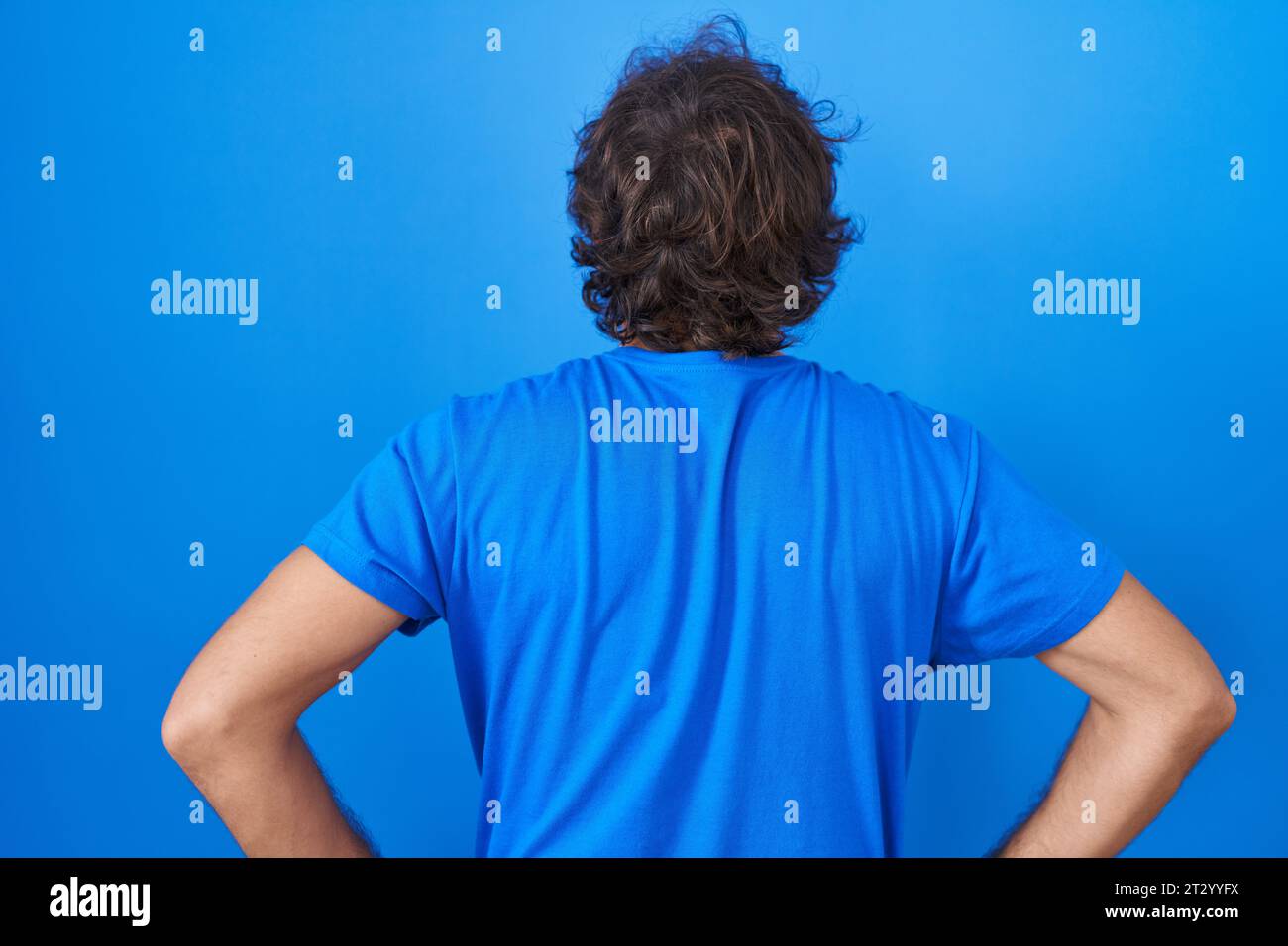 Hispanic young man standing over blue background standing backwards ...
