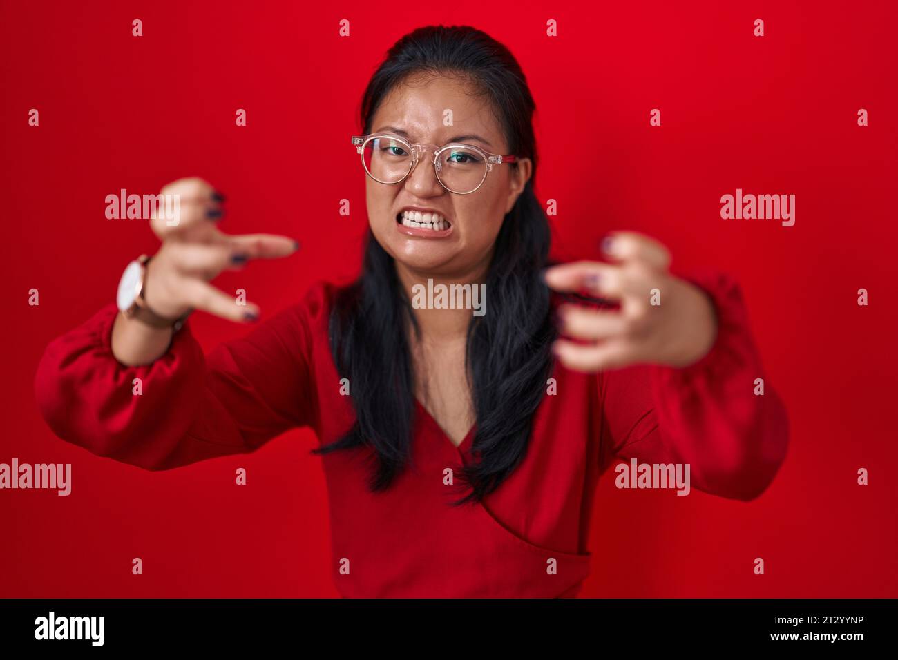 Asian young woman standing over red background shouting frustrated with ...
