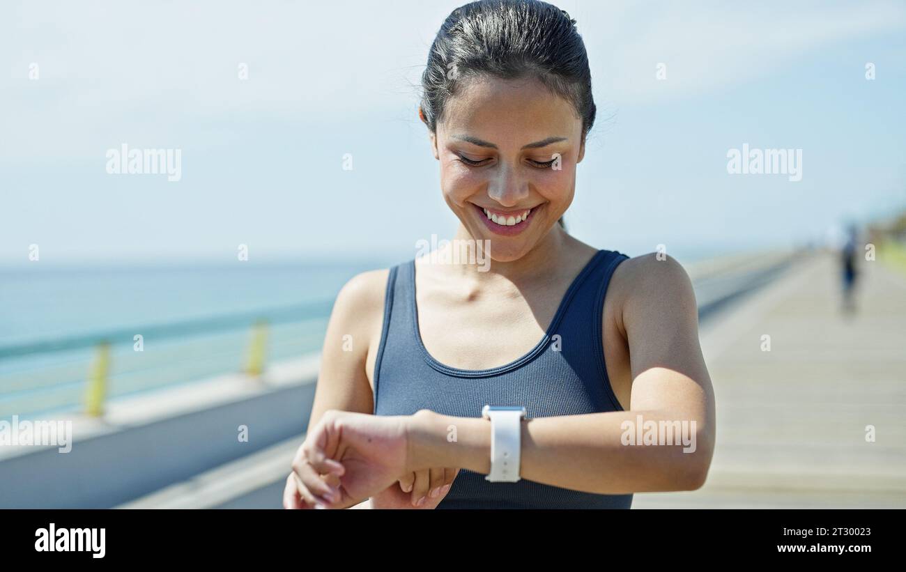 Young beautiful hispanic woman wearing sportswear looking smartwatch ...