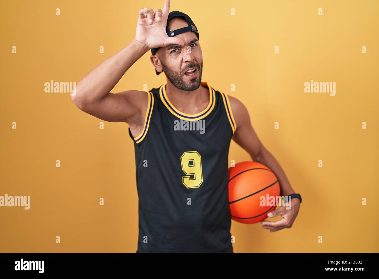 Middle age bald man holding basketball ball over yellow background ...