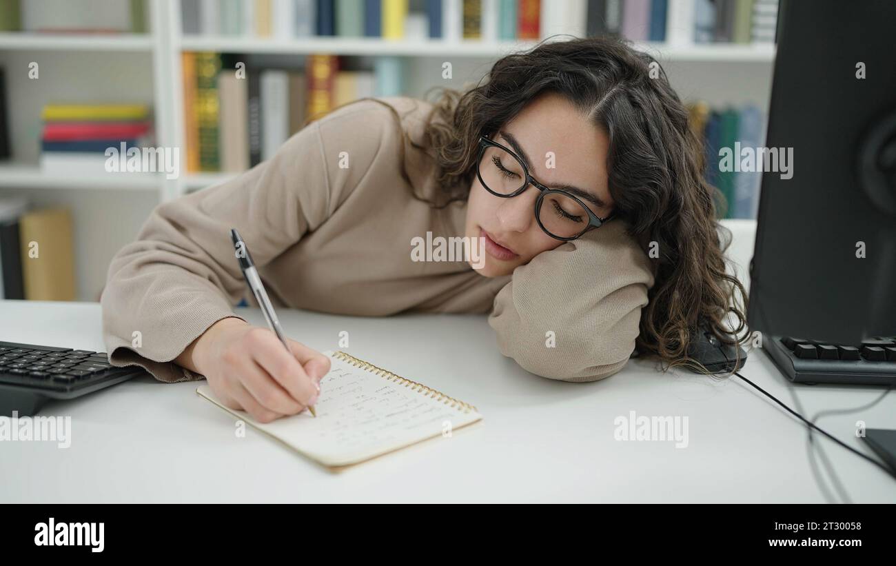 Young beautiful hispanic woman student writing notes tired at library ...