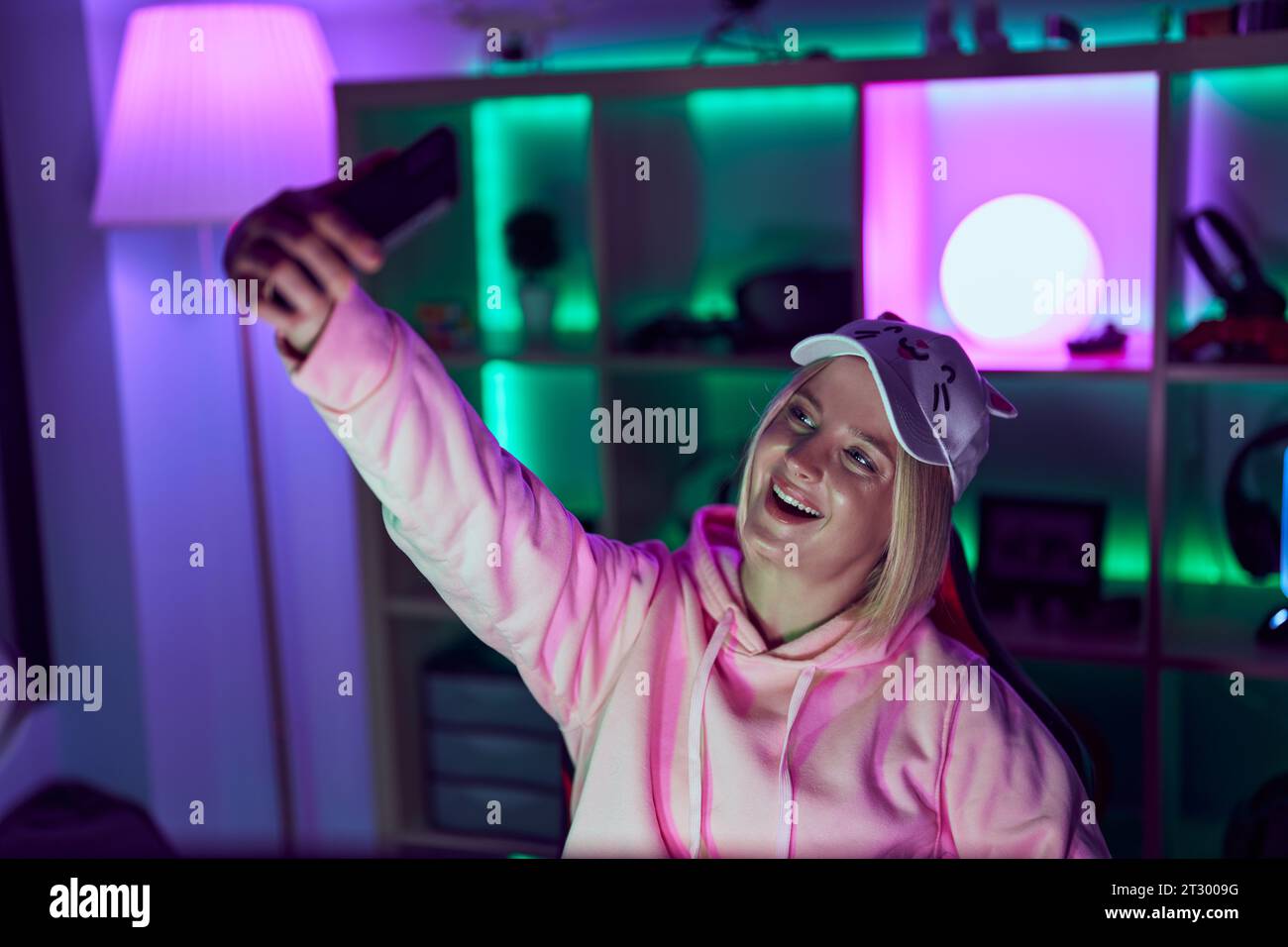 Young blonde woman streamer make selfie by smarpthone at gaming room ...