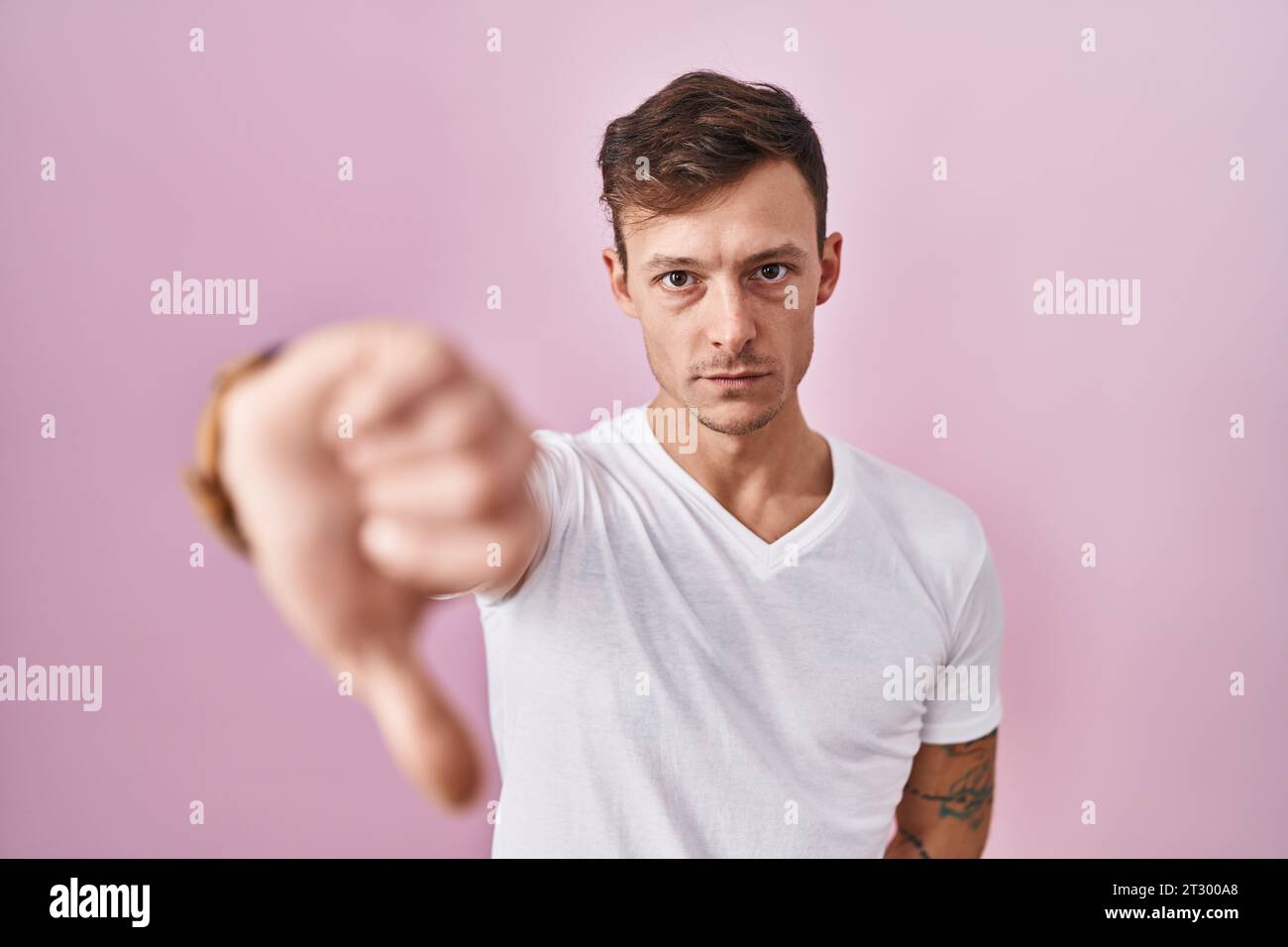 Caucasian man standing over pink background looking unhappy and angry ...