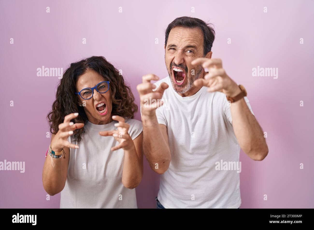 Middle age hispanic couple together over pink background shouting ...