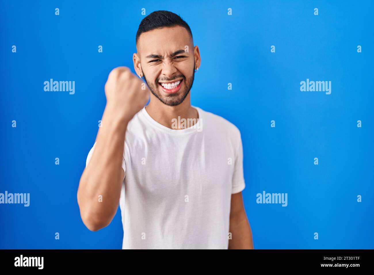 Young hispanic man standing over blue background angry and mad raising ...