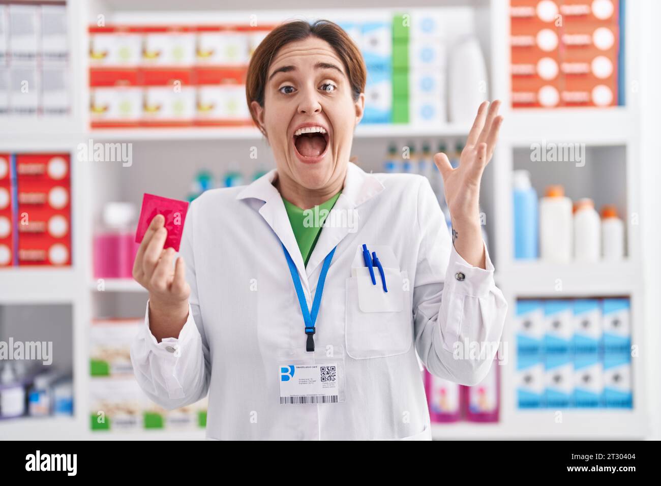 Brunette woman working at pharmacy drugstore holding condom celebrating ...