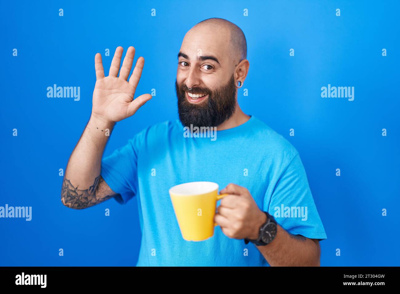Young hispanic man with beard and tattoos drinking a cup of coffee ...