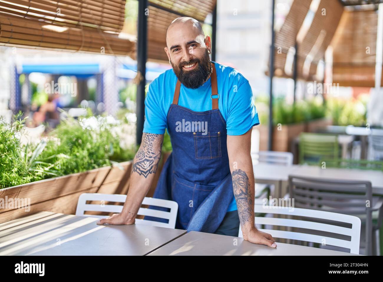 Young bald man waiter smiling confident standing at coffee shop terrace ...