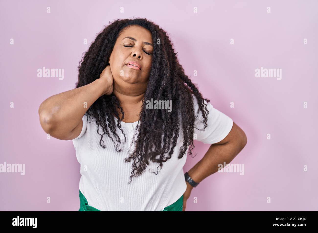 Plus size hispanic woman standing over pink background suffering of ...