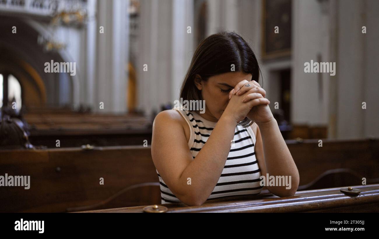 Young beautiful hispanic woman praying on a church bench at Augustinian ...