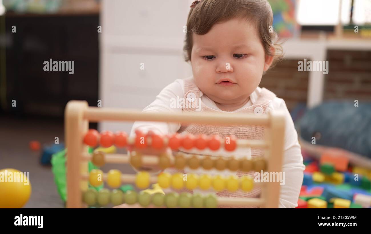 Adorable toddler playing with abacus sitting on floor at kindergarten ...