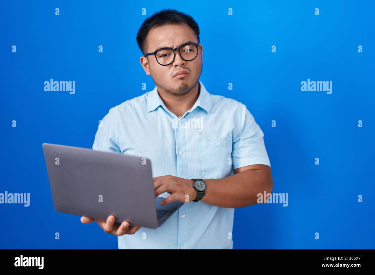 Chinese young man using computer laptop skeptic and nervous, frowning ...