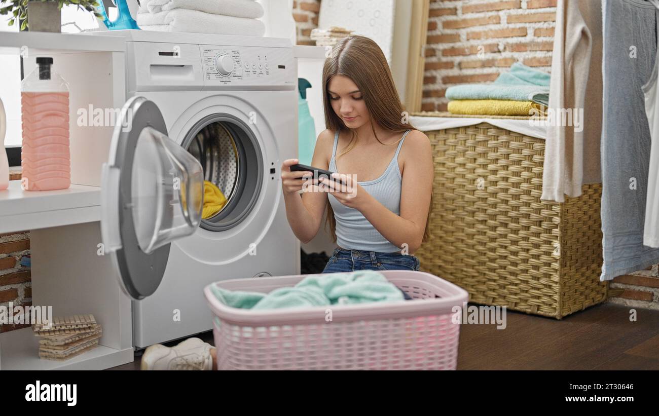 Young beautiful girl washing clothes playing video game at laundry room ...