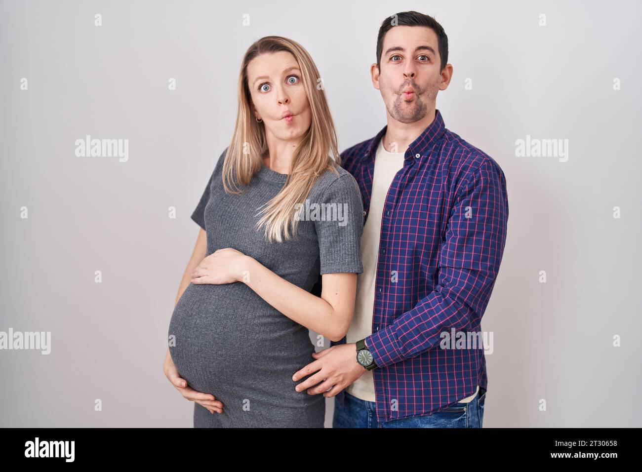 Young couple expecting a baby standing over white background making ...