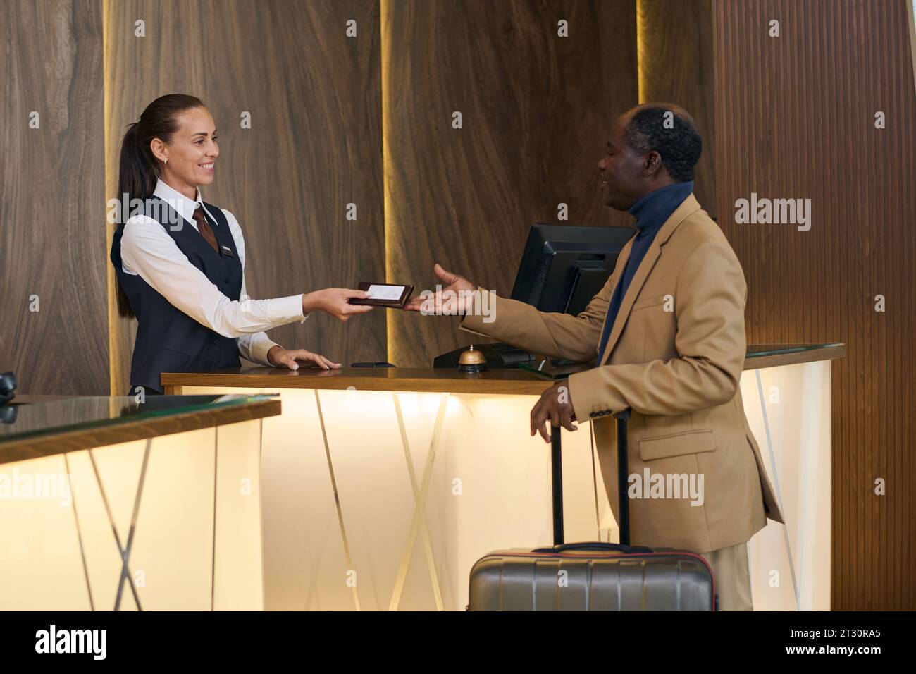 Receptionist giving key from room to guest during his check-in in the ...