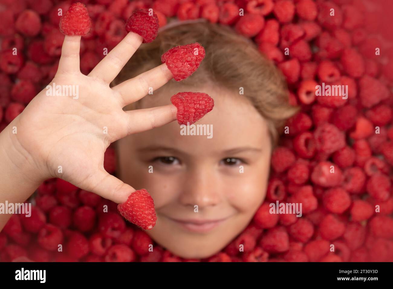Cute little girl eats raspberries berries. Kid eating vitamins. Close ...