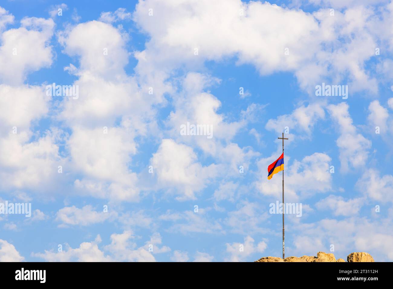 Armenian flag on flagpole with cross on top of hill and blue sky with ...