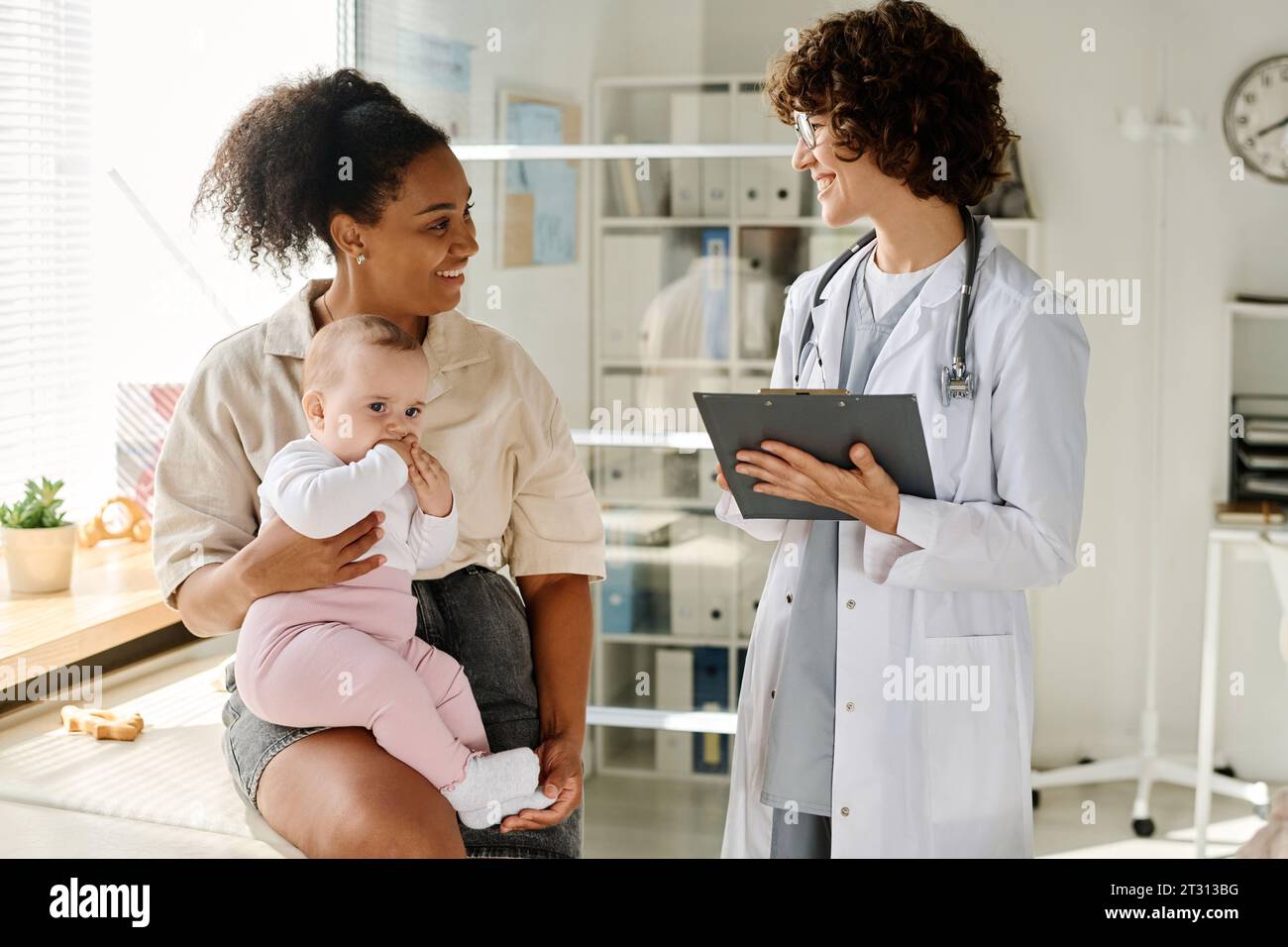 Pediatrician talking to mom and writing prescription while she visit to ...