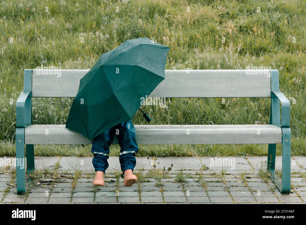 A little girl is hiding from the rain under an umbrella. She is sitting ...