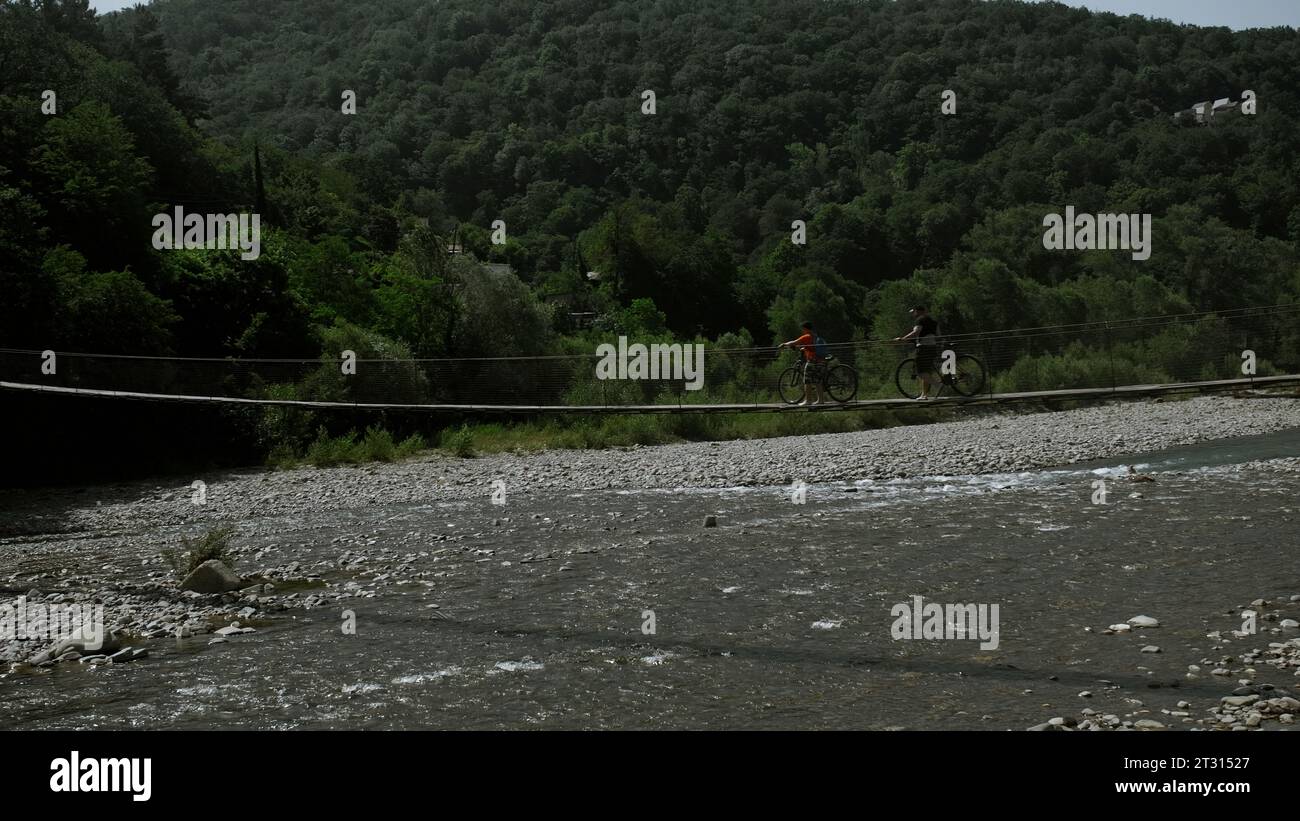 Hikers walk with bicycles on a bridge that crosses wild and beautiful ...