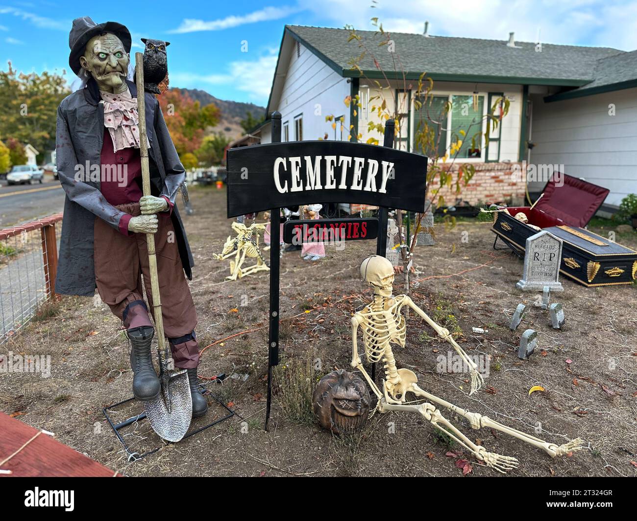 Halloween decorations are in a front yard. They include a cemetery sign ...