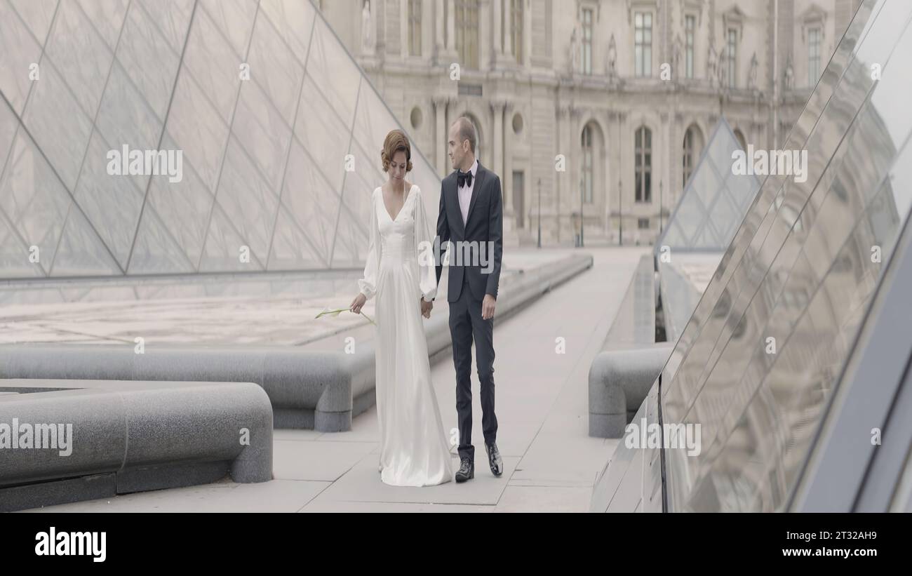 Walking bride and groom with a glass facade Louvre pyramid. Action ...