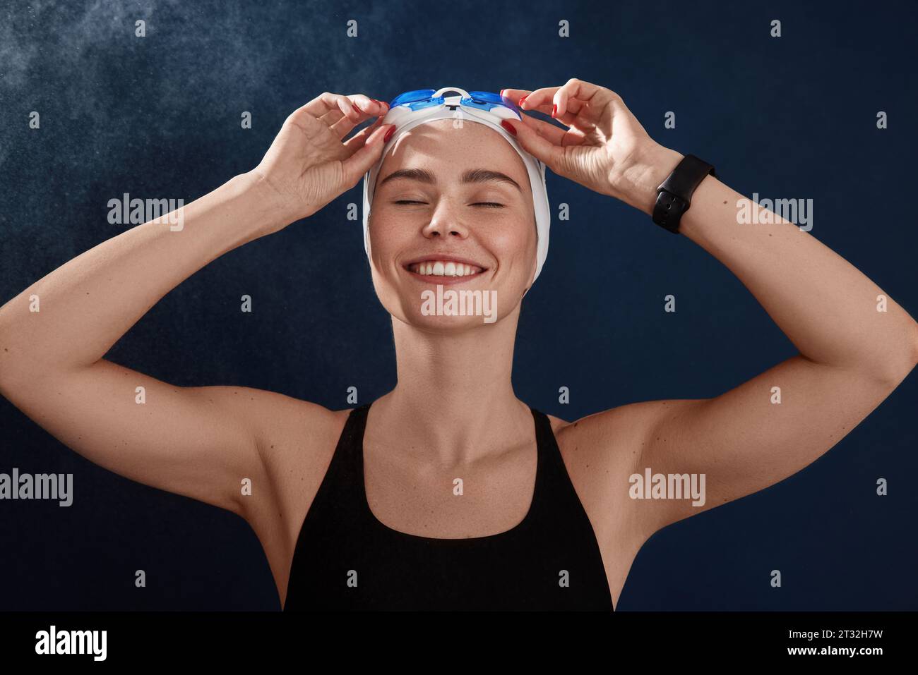 Young smiling female swimmer with closed eyes adjusting goggles ...