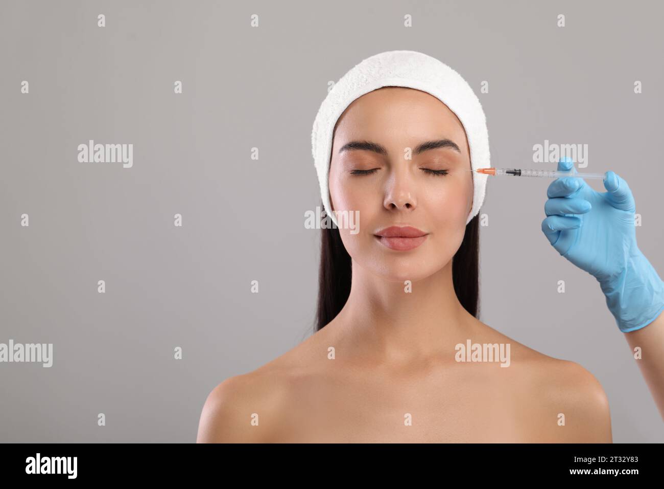 Doctor giving facial injection to young woman on light grey background ...