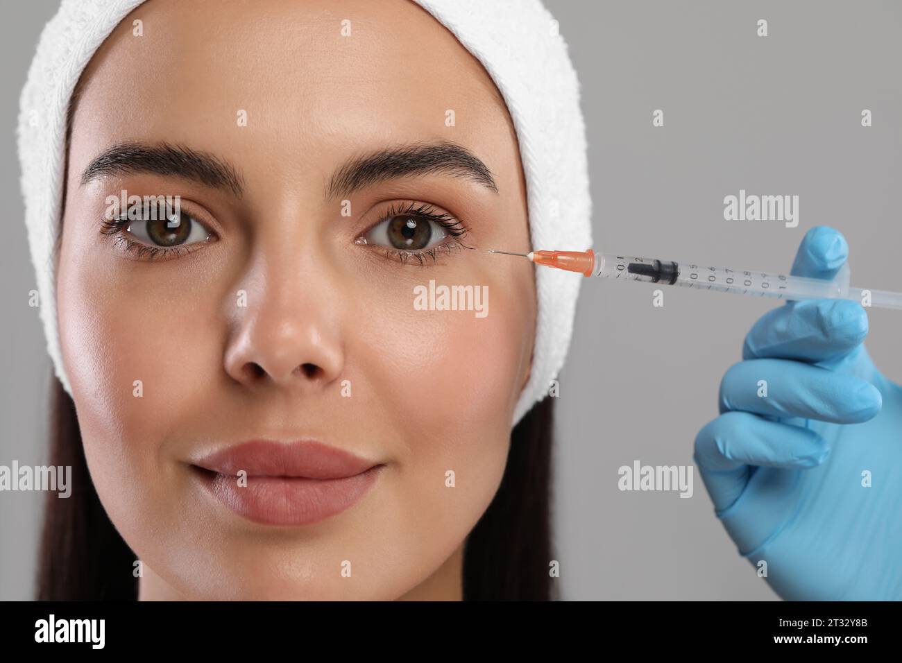 Doctor giving facial injection to young woman on light grey background ...