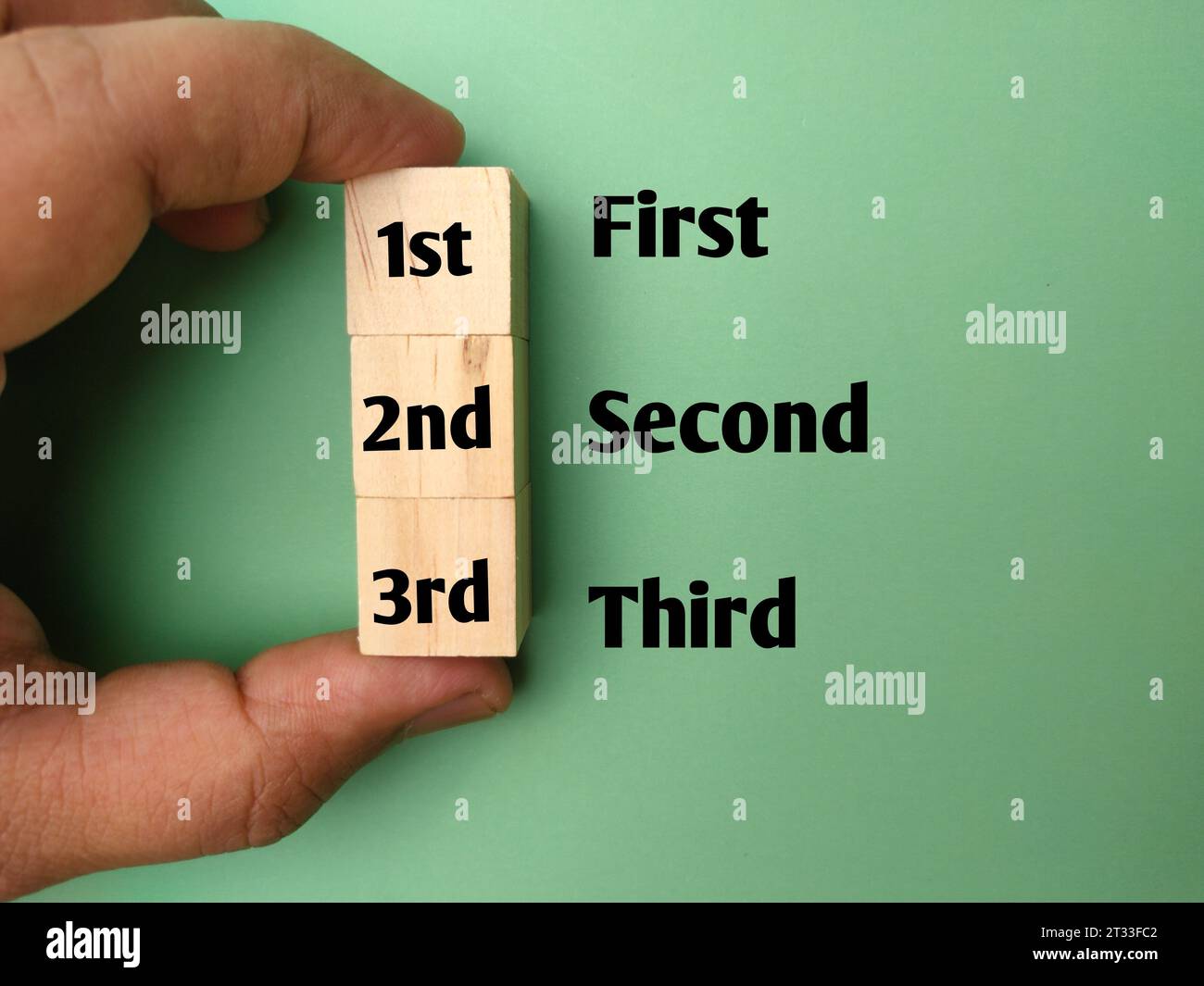 Hand holding wooden block with text First Second Third on green ...