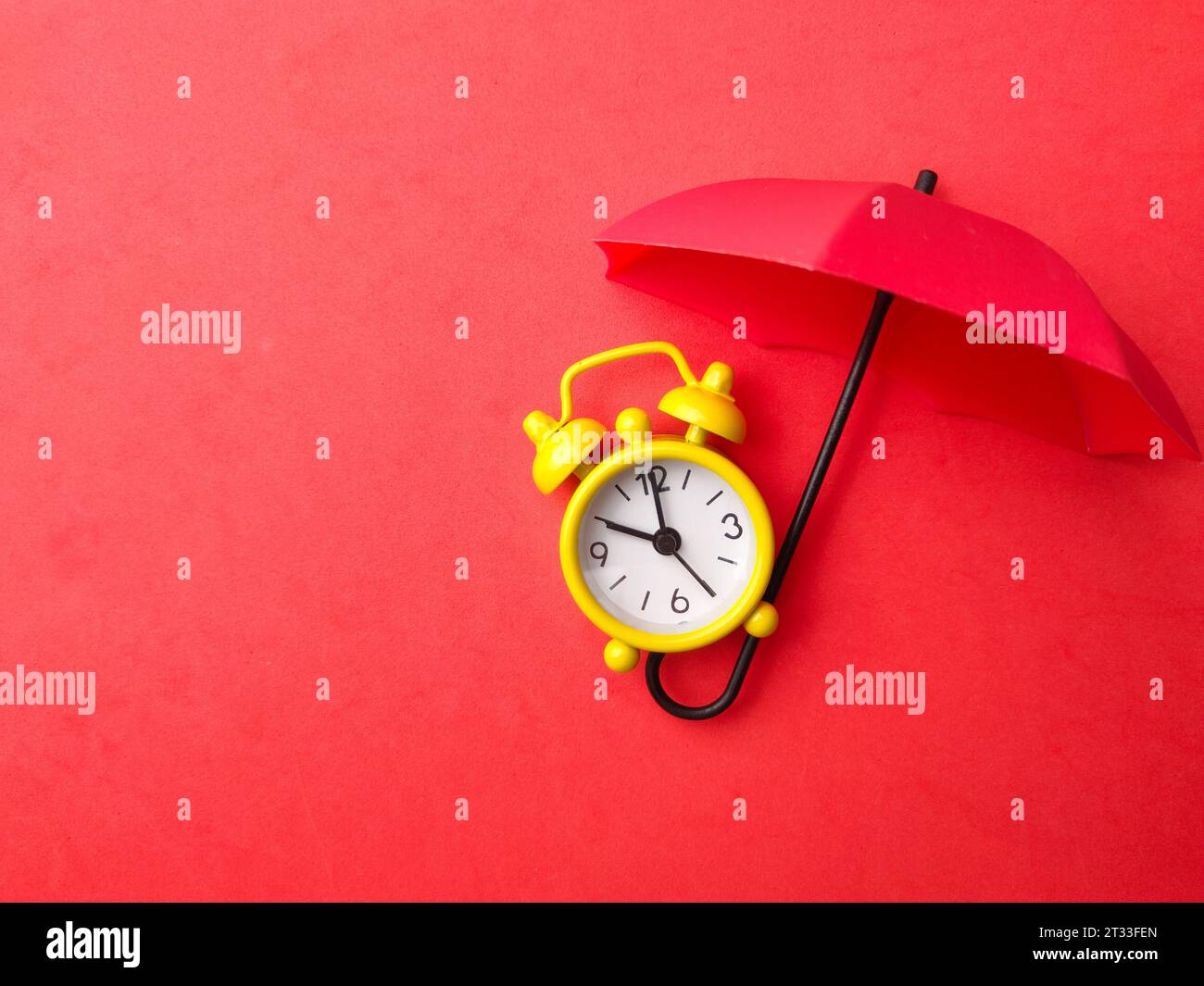 A yellow alarm clock with red umbrella on a red background with copy ...