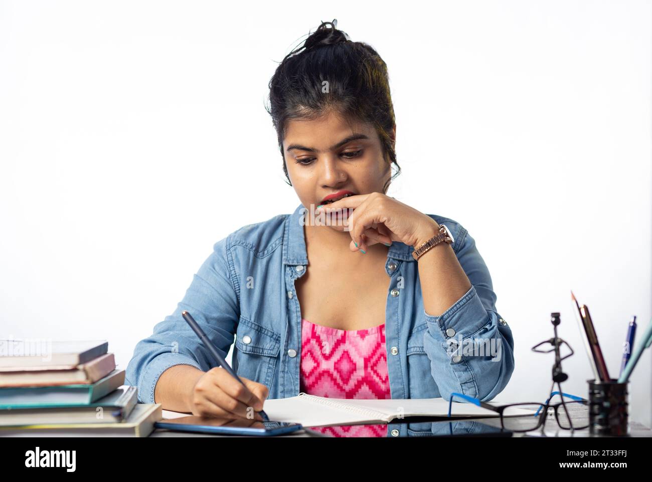 A pretty young Indian college student studying and biting finger on ...