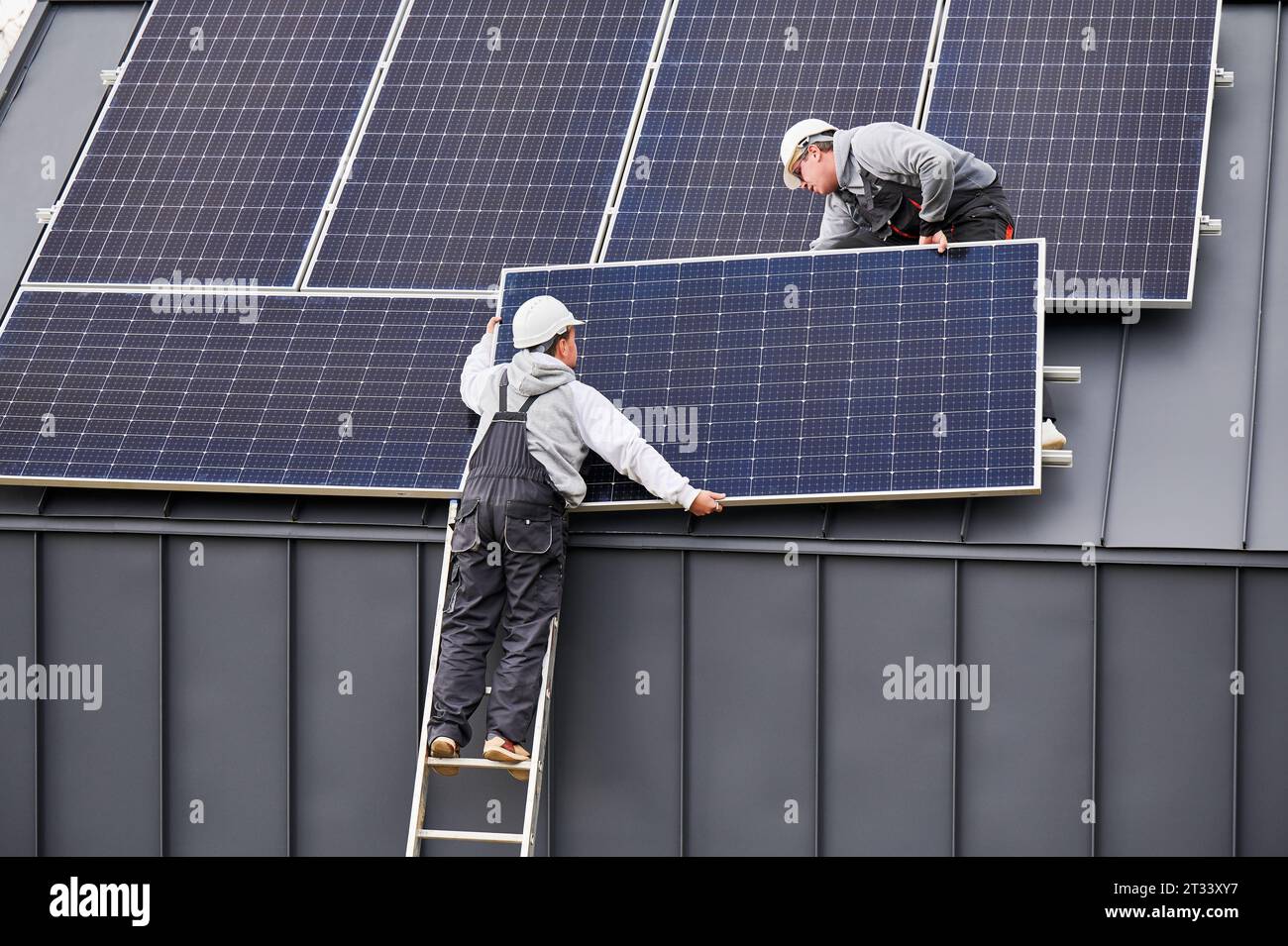 Engineers connecting cables while installing photovoltaic solar panels on roof of house. Workers ...