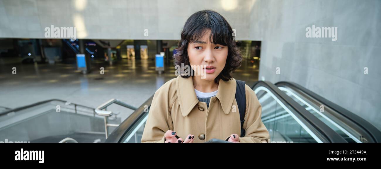 People in city. Portrait of korean girl standing on escalator, looks ...