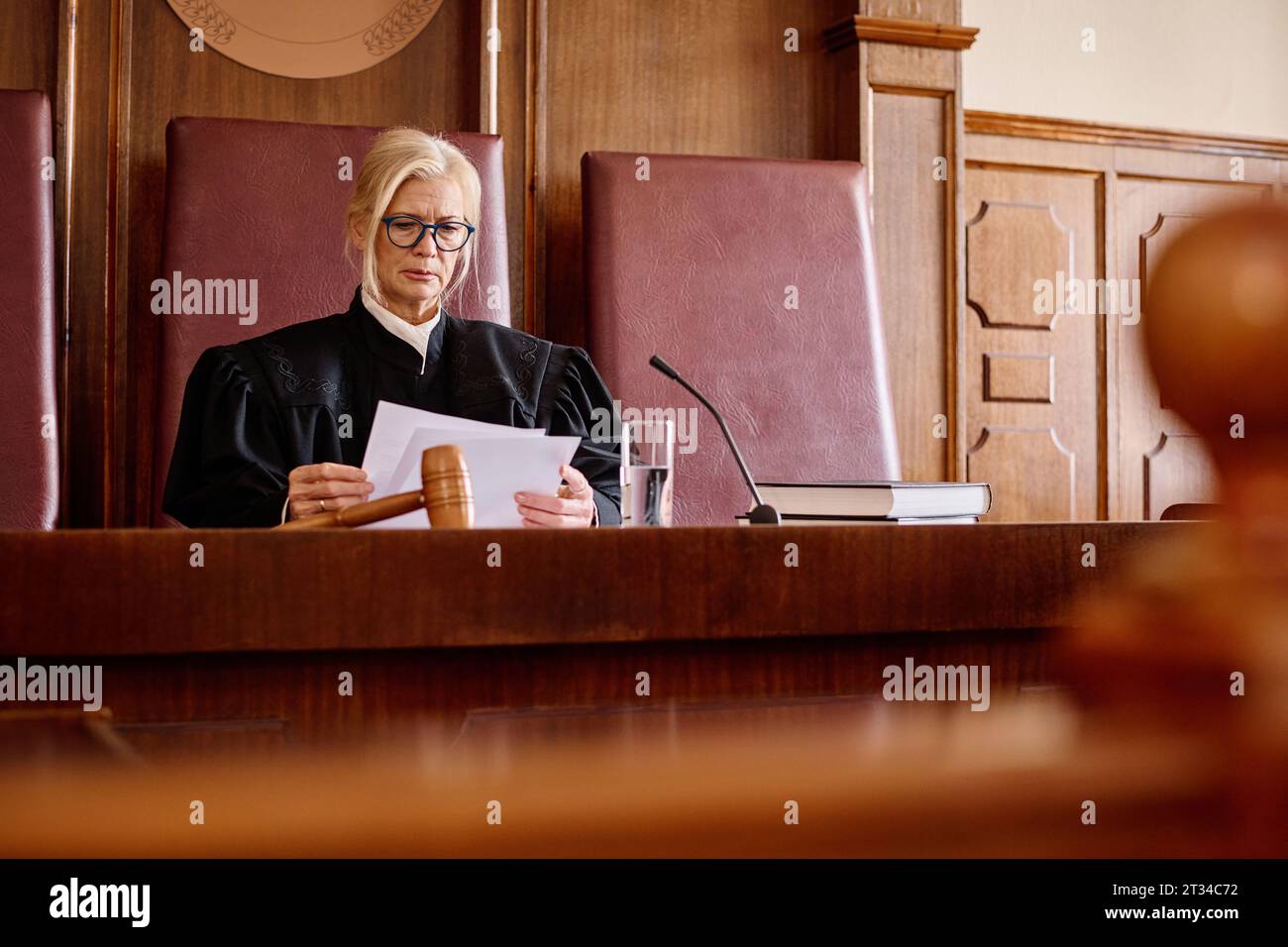 Experienced female judge in black gown reading juridical paper ...