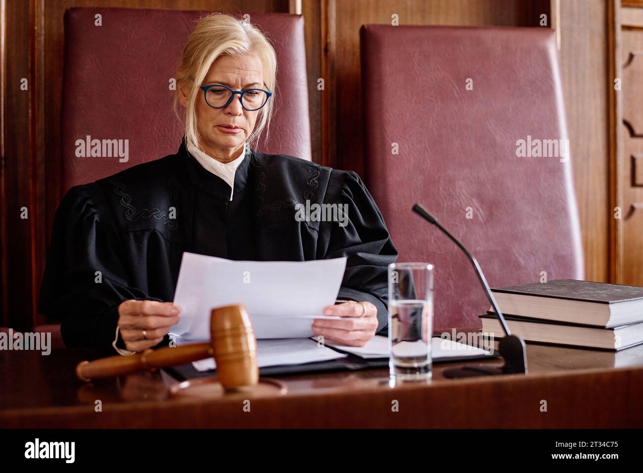 Serious blond female judge in black mantle looking through paper ...