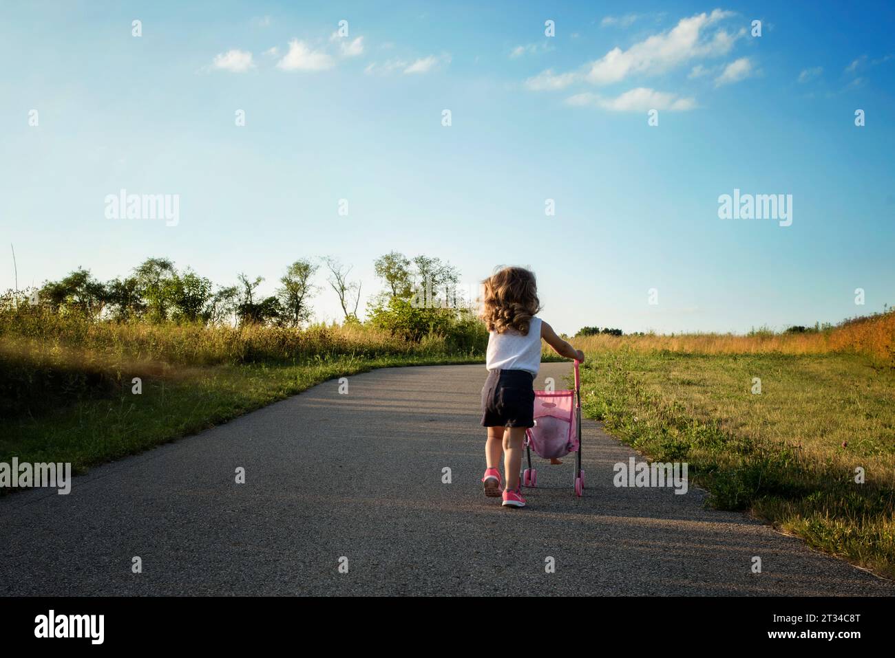 Little girl pushing pink stroller outside in summer Stock Photo - Alamy