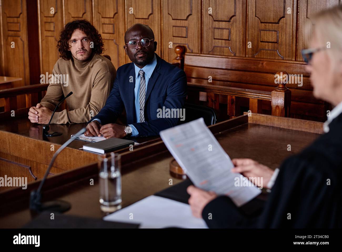 Two young intercultural male attorneys looking at female judge with ...