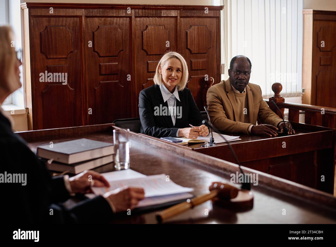 Smiling mature female attorney and her African American colleague looking at judge while ...