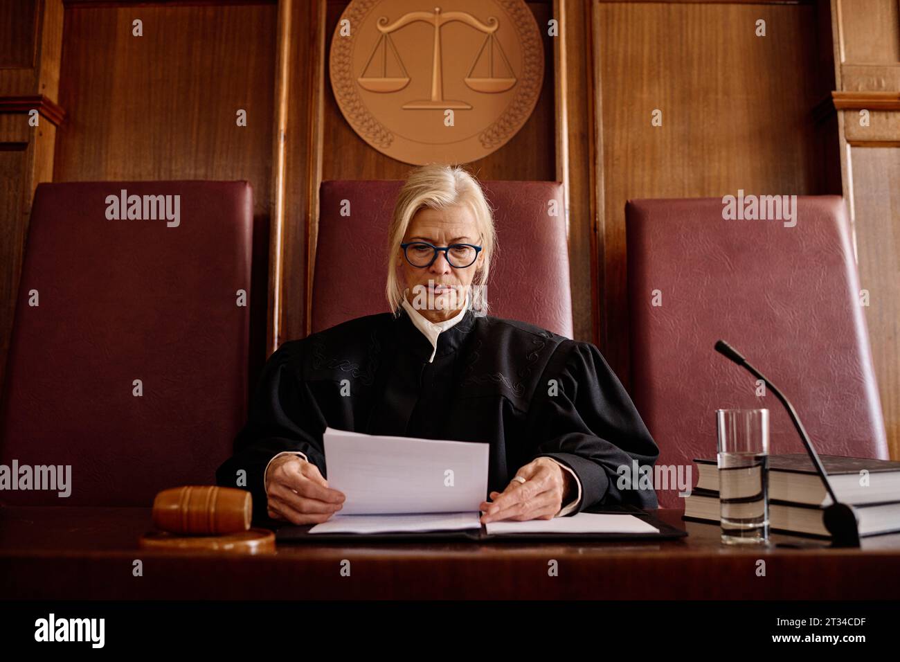 Confident mature female judge in black mantle looking through documents ...