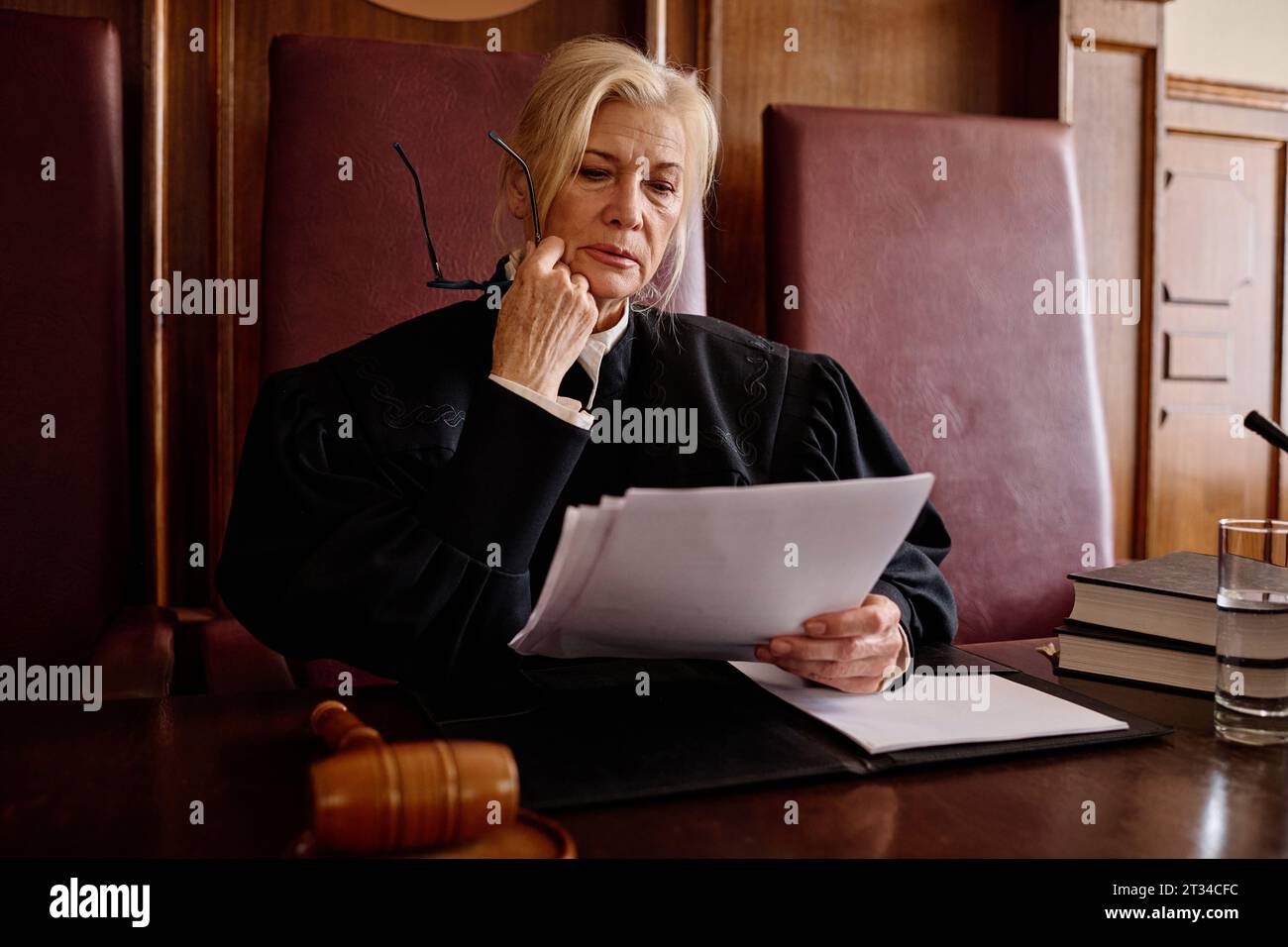 Serious blond woman in black mantle looking through paper documents ...