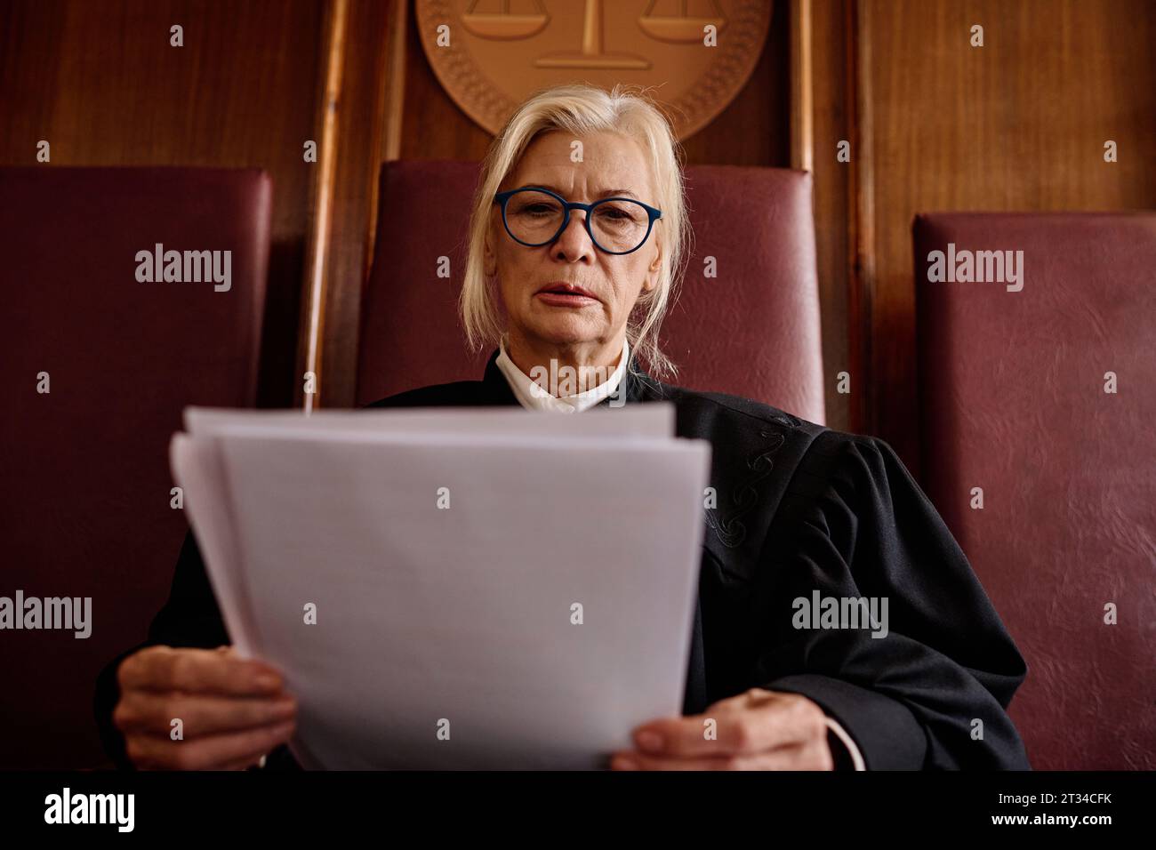 Serious blond female impartial judge reading juridical document during ...