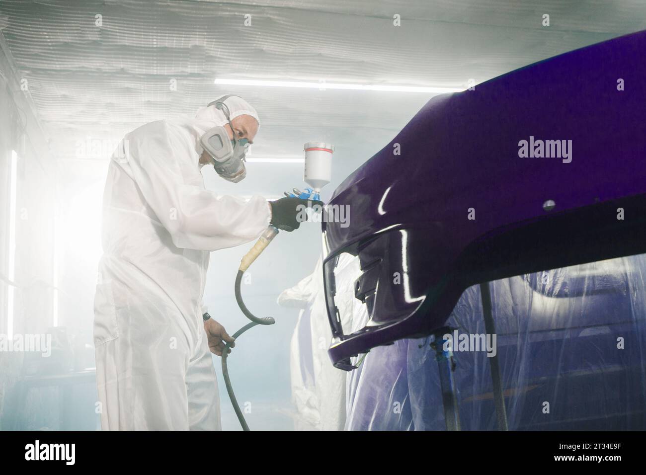 Male automobile repairman painter in protective workwear and respirator ...