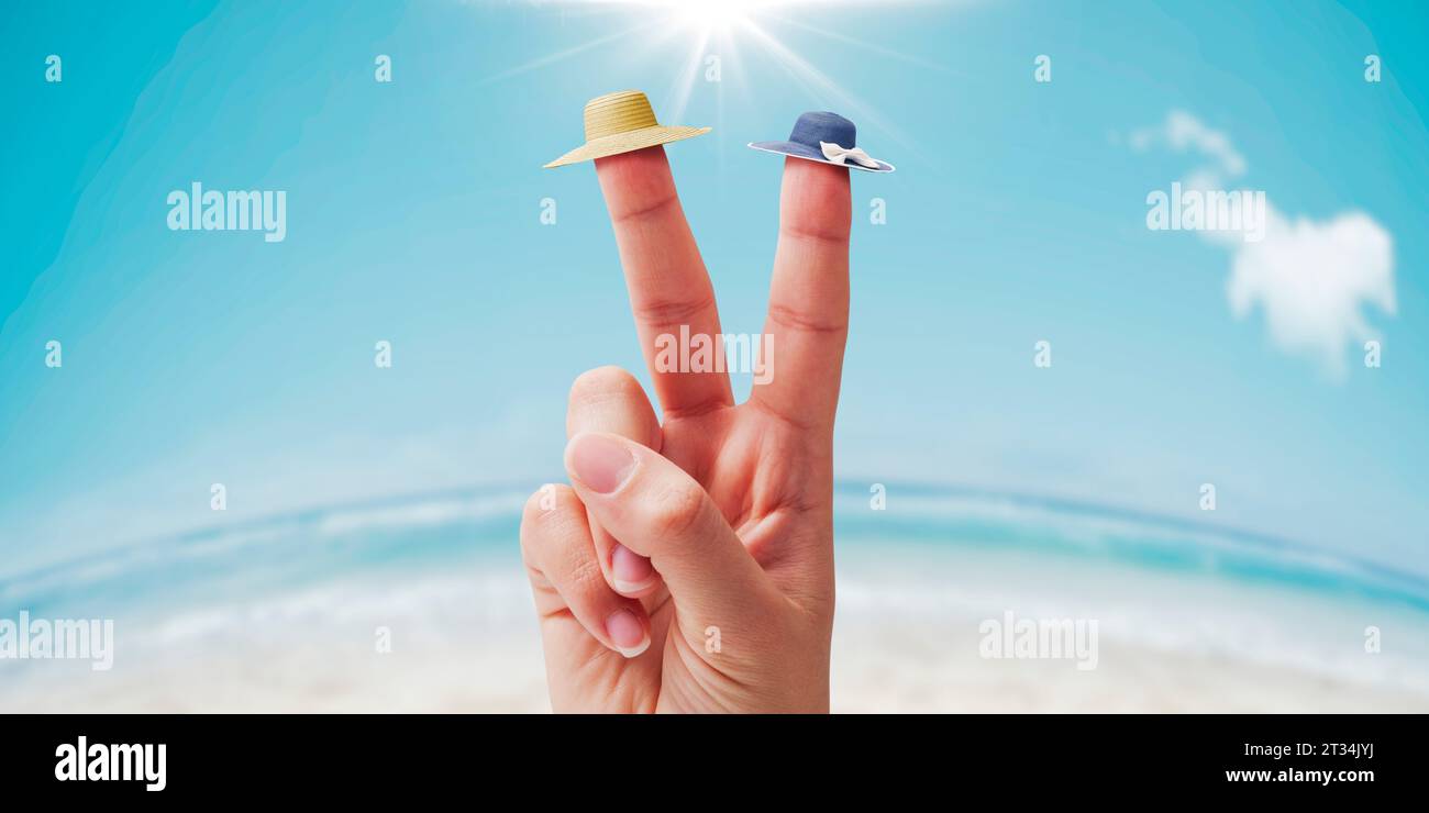 Hand making a V sign and wearing hats on two fingers, beach in the ...