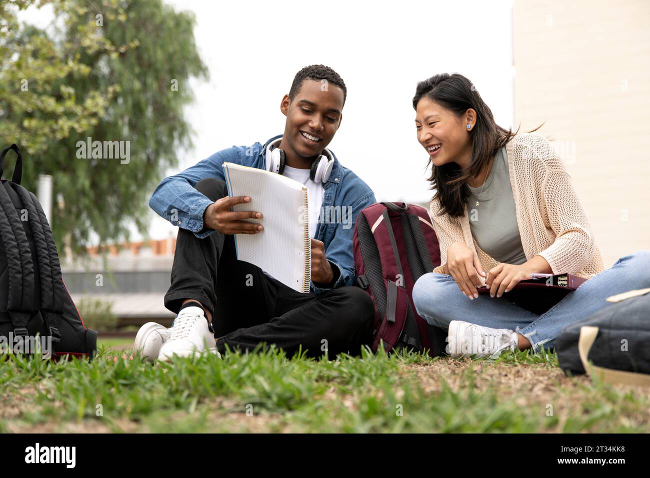 Diverse couple of students sitting outside reading documents.Two young ...