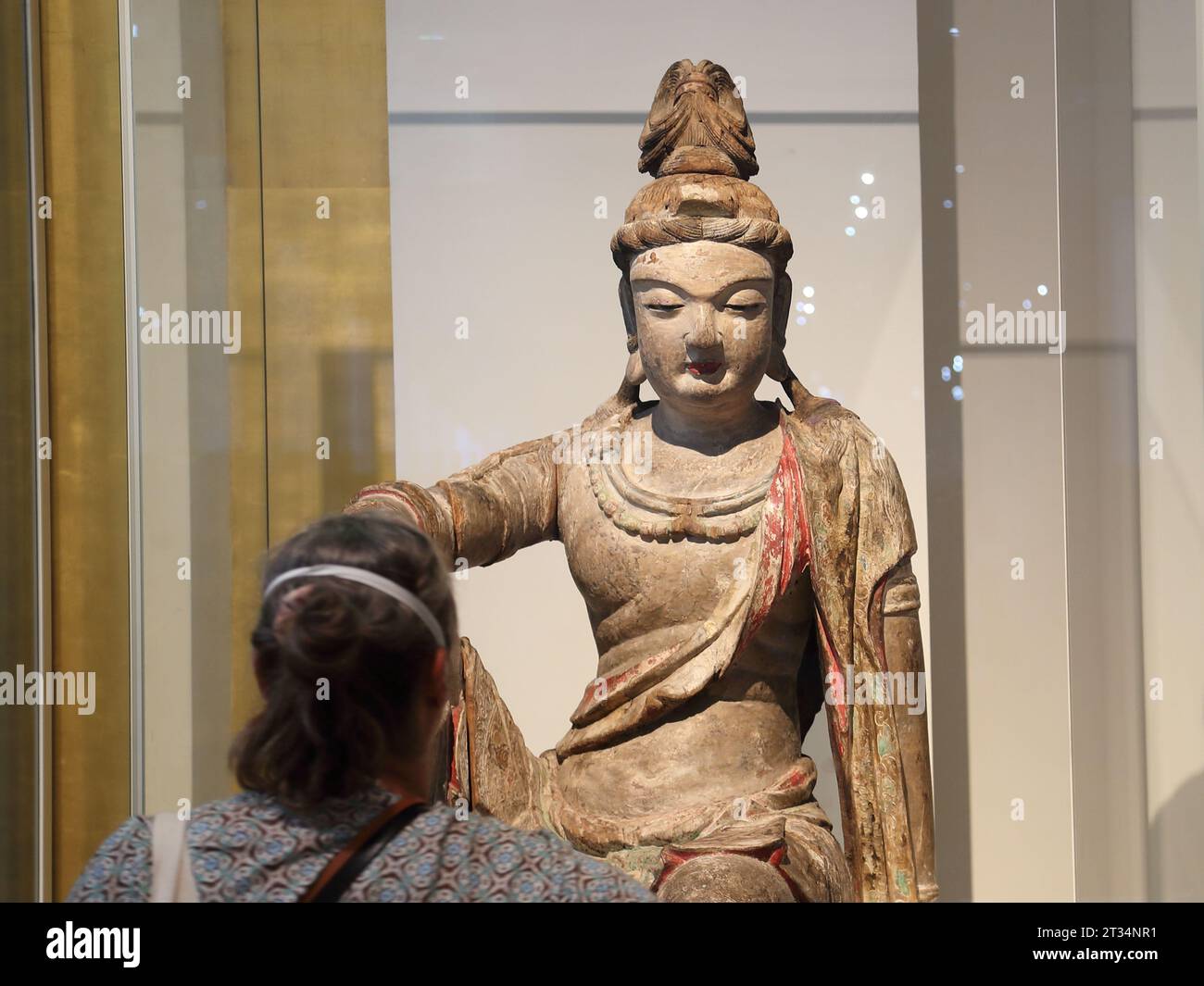 A woman studies a Chinese devotional painted wooden image of Guanyin ...