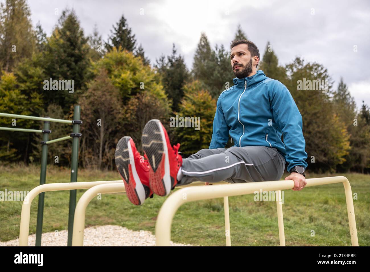 A young athlete trains on the bars, raises his legs parallel to the ...